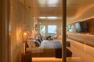Quarto moderno com cama grande, sofá, televisão na parede e vista para o exterior.