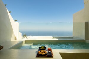 Uma varanda com vista para o mar, uma banheira de hidromassagem e um tabuleiro com comida e bebidas.