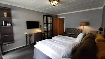 Quarto de hotel com cama, escrivaninha, cadeira, televisão, guarda-roupa e abajur.