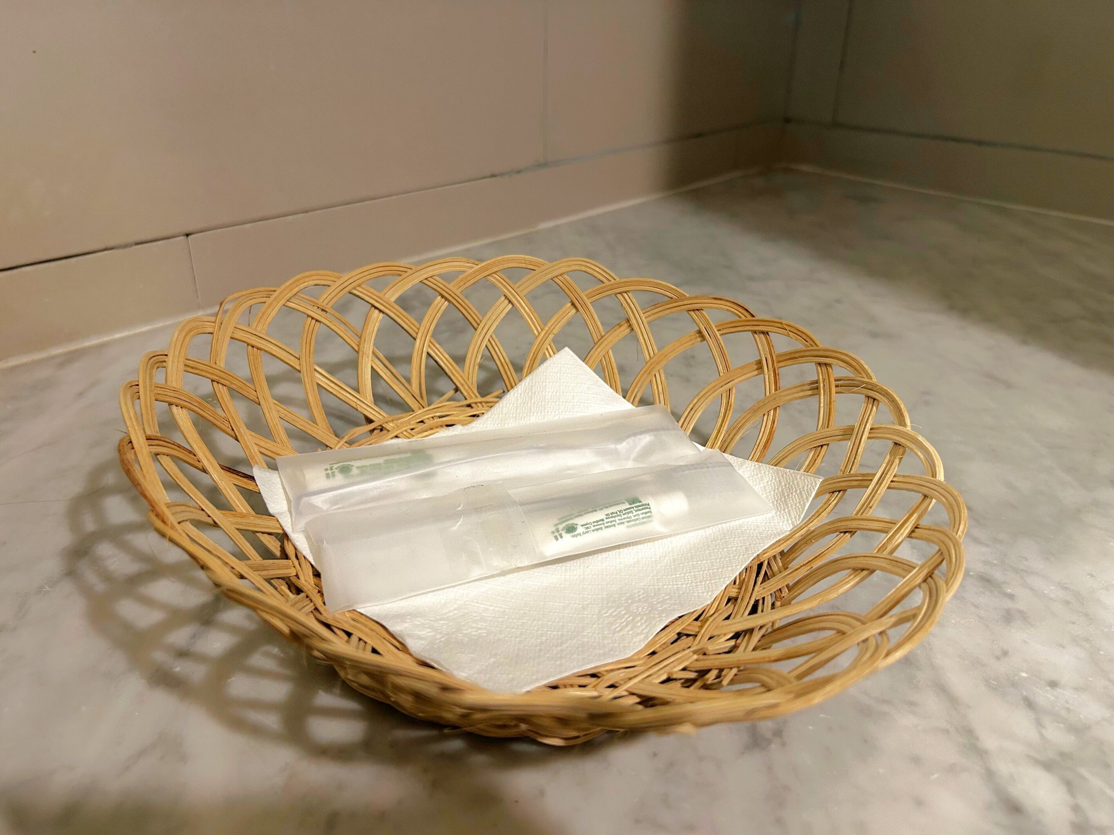 Uma cesta de palha com uma caixa de lenços, colocada em um chão de mármore.