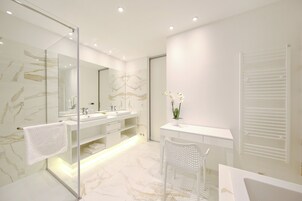 Uma casa de banho moderna com cabine de duche em vidro, toucador branco com espelho e uma cadeira branca.
