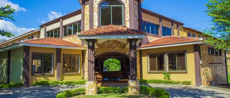 Uma casa grande de dois andares com fachada de pedra, várias janelas e um arco central.