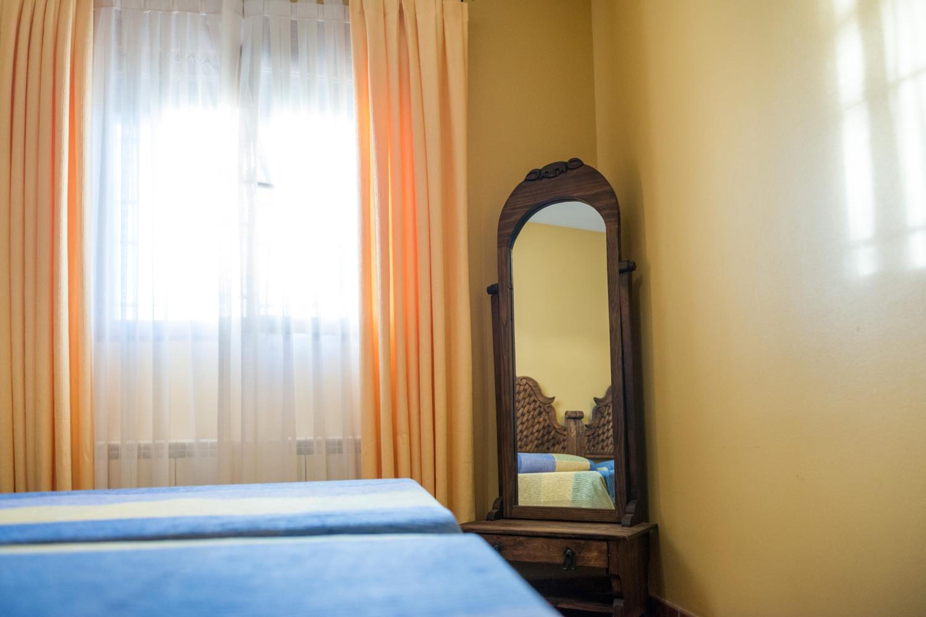Quarto com cama, cómoda de madeira e espelho refletindo uma cama com colcha azul e branca.
