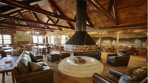 Um interior rústico com lareira de pedra, sofás de couro, mesas de madeira e um grande mural na parede.