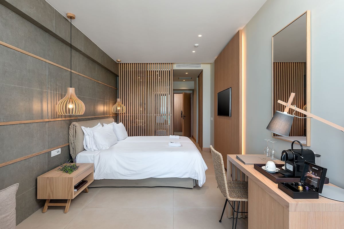 Quarto de hotel moderno com uma cama grande, mesa de cabeceira e escrivaninha com cafeteira.