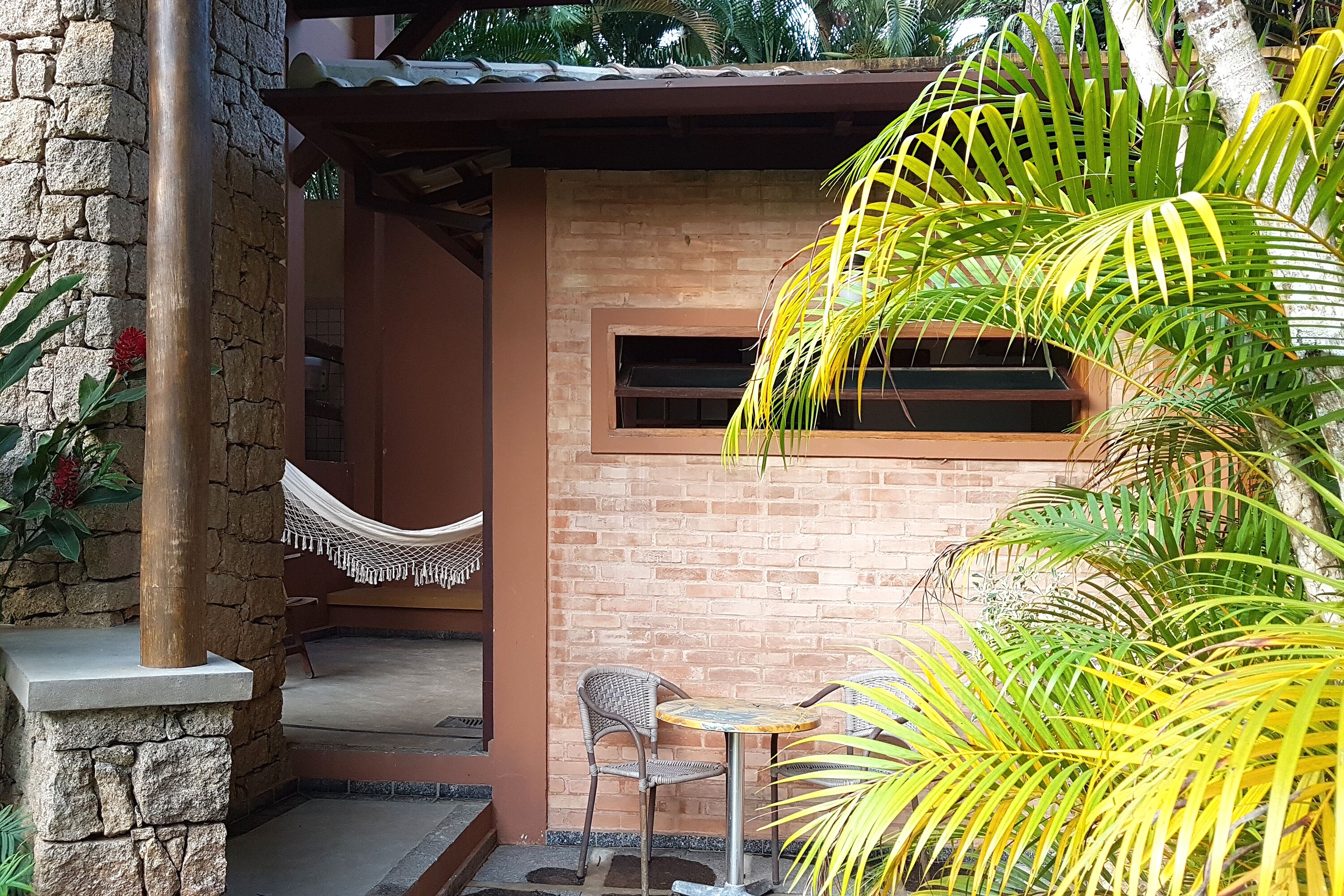 Área de pátio com parede de tijolos, rede e uma pequena mesa com cadeira.