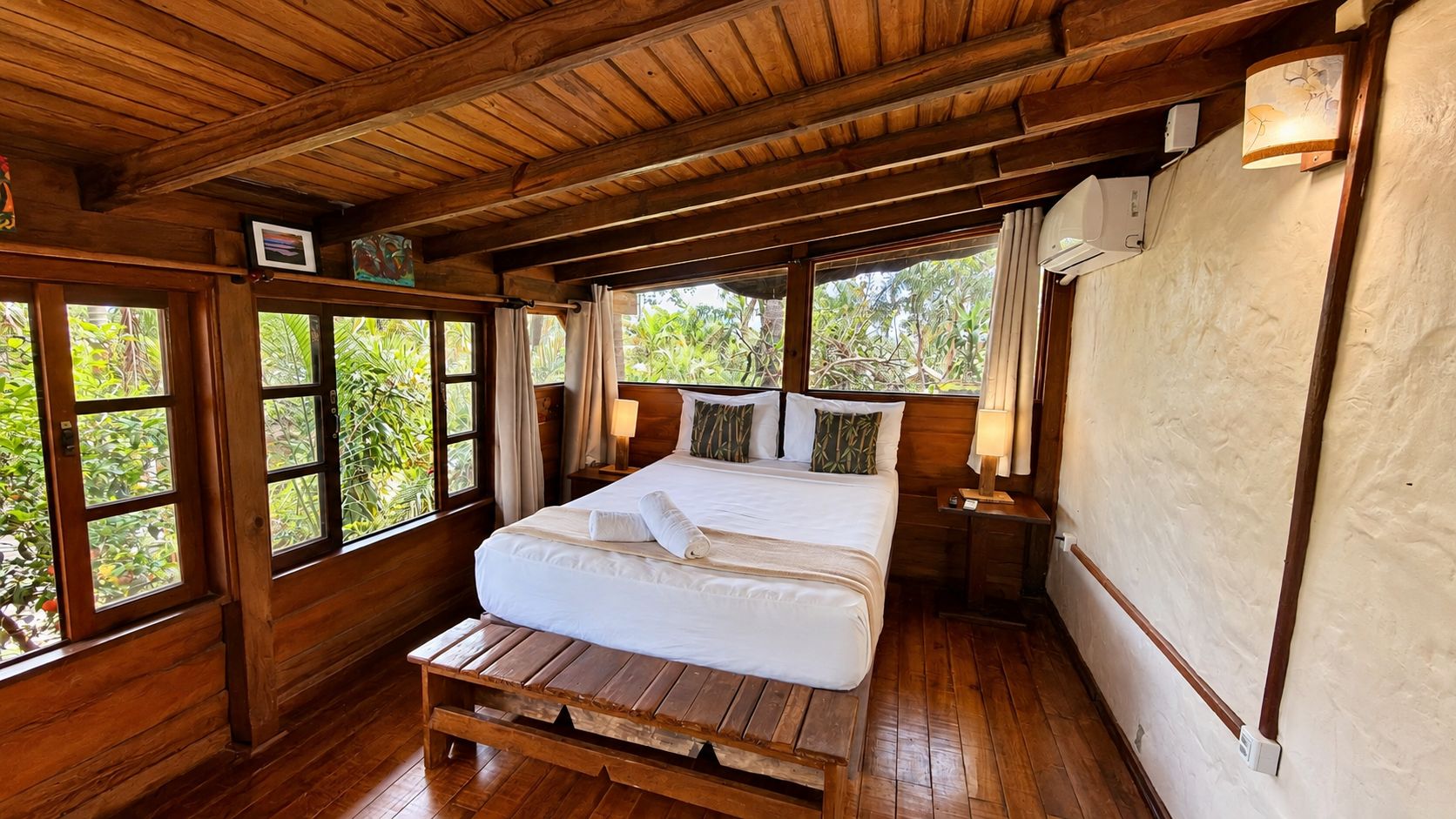 Quarto de madeira com uma cama, janelas e um banco.