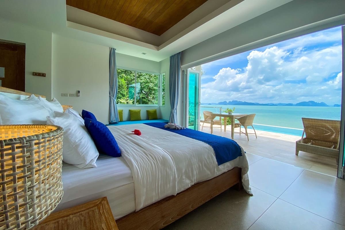Quarto com uma cama grande, mesa de cabeceira de vime e vista para o mar.