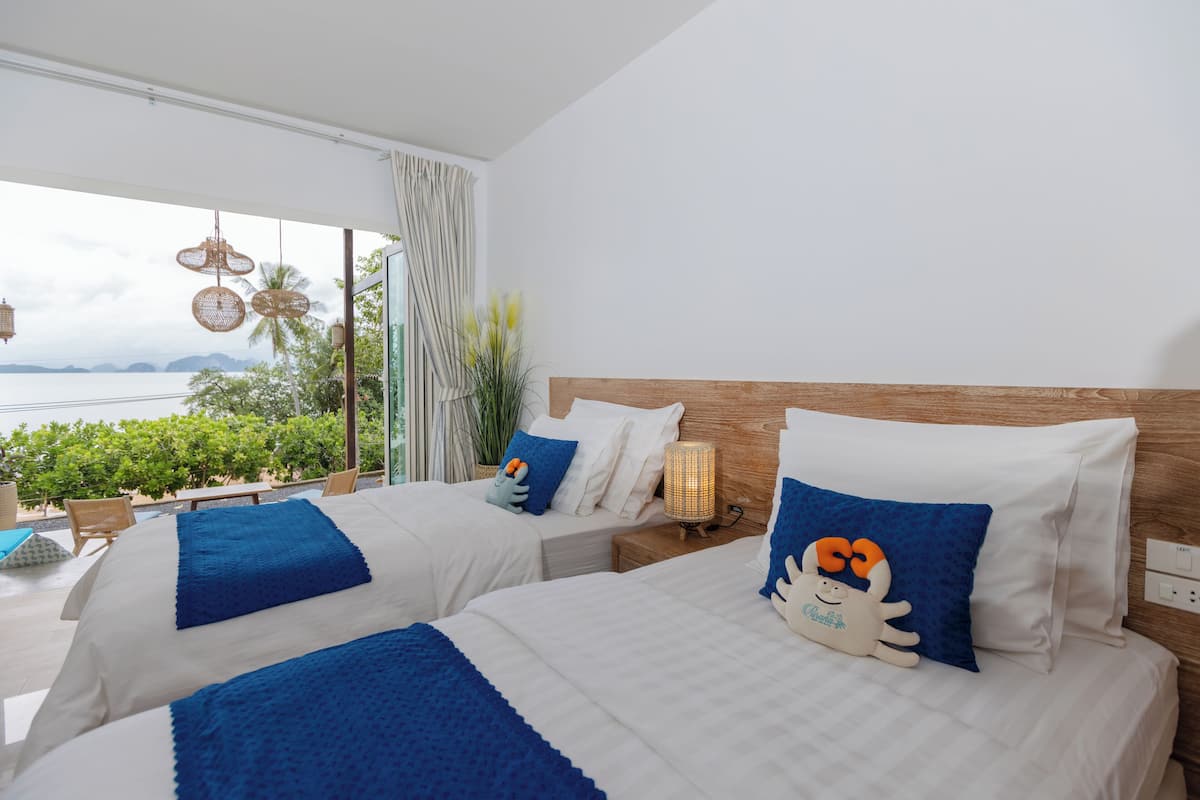 Quarto de hotel com duas camas, vista para o mar e varanda com área de estar ao ar livre.