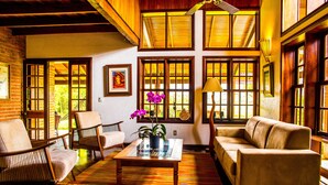 Uma sala de estar acolhedora com um sofá, cadeiras, uma mesa de centro e um vaso de planta.