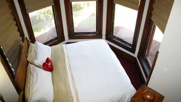 Quarto com uma cama grande, cabeceira de madeira e vista para o exterior através de uma janela.