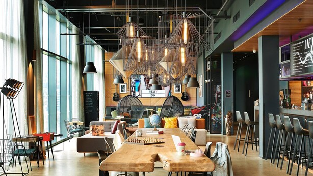 Um café moderno com uma longa mesa de madeira, várias luminárias pendentes e um espaço de bar com banquetas.