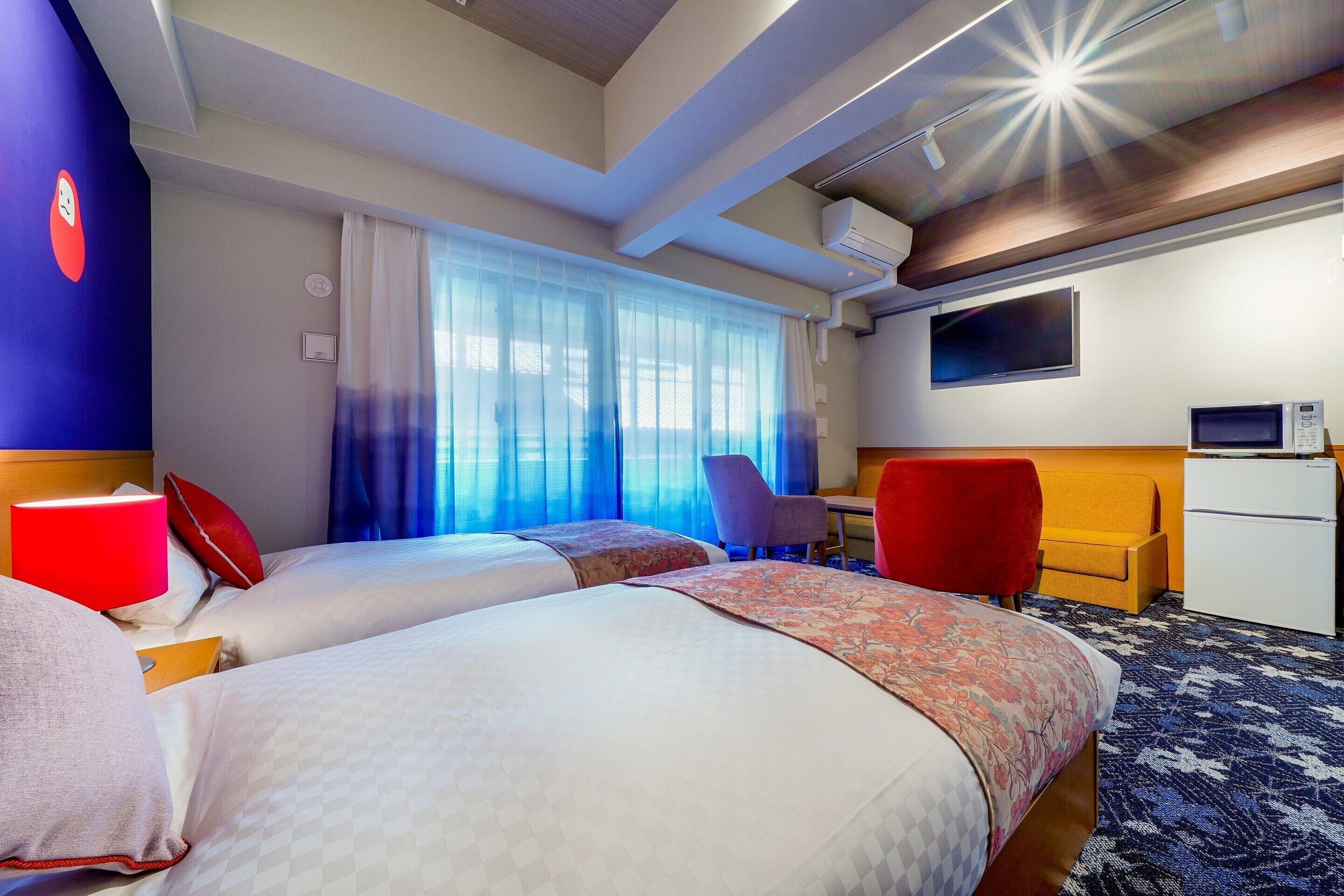 Quarto de hotel com duas camas, uma escrivaninha, uma cadeira, uma televisão e um micro-ondas.