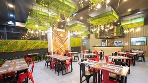 Um restaurante com várias mesas e cadeiras, área de bar e decoração com folhagem verde nas paredes e no teto.