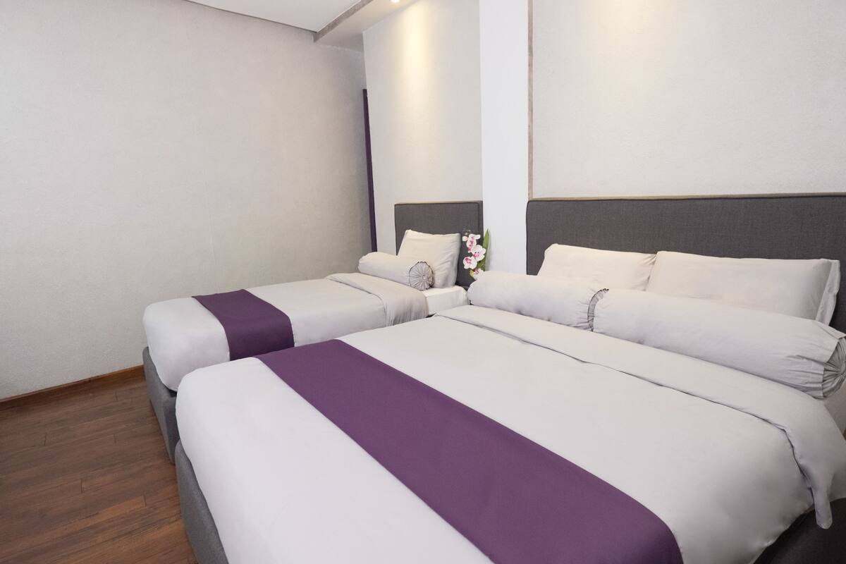 Quarto de hotel com duas camas, cada uma com roupa de cama branca e detalhes em roxo.