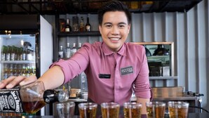 Um bartender servindo uma bebida num copo em um bar, com vários copos sobre o balcão.