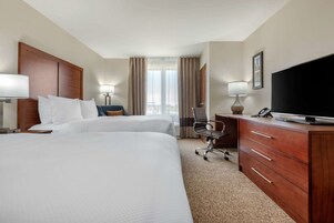 Quarto de hotel com duas camas, uma escrivaninha com televisão, uma cadeira e um abajur.