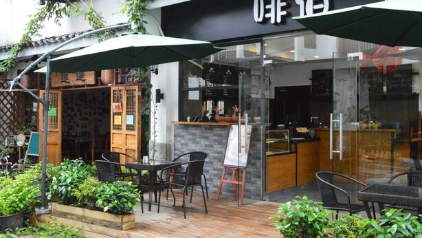 Café ao ar livre com mobiliário de madeira e plantas verdes.