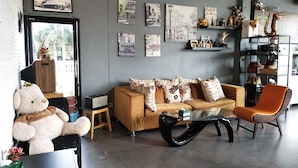 Uma sala de estar moderna com um sofá, mesa de centro e uma poltrona. Prateleiras fixadas na parede exibem objetos decorativos e uma grande janela oferece vista para o exterior.