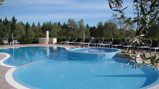 Uma piscina ampla e translúcida com várias pistas, rodeada por espreguiçadeiras e um deck de pedra.
