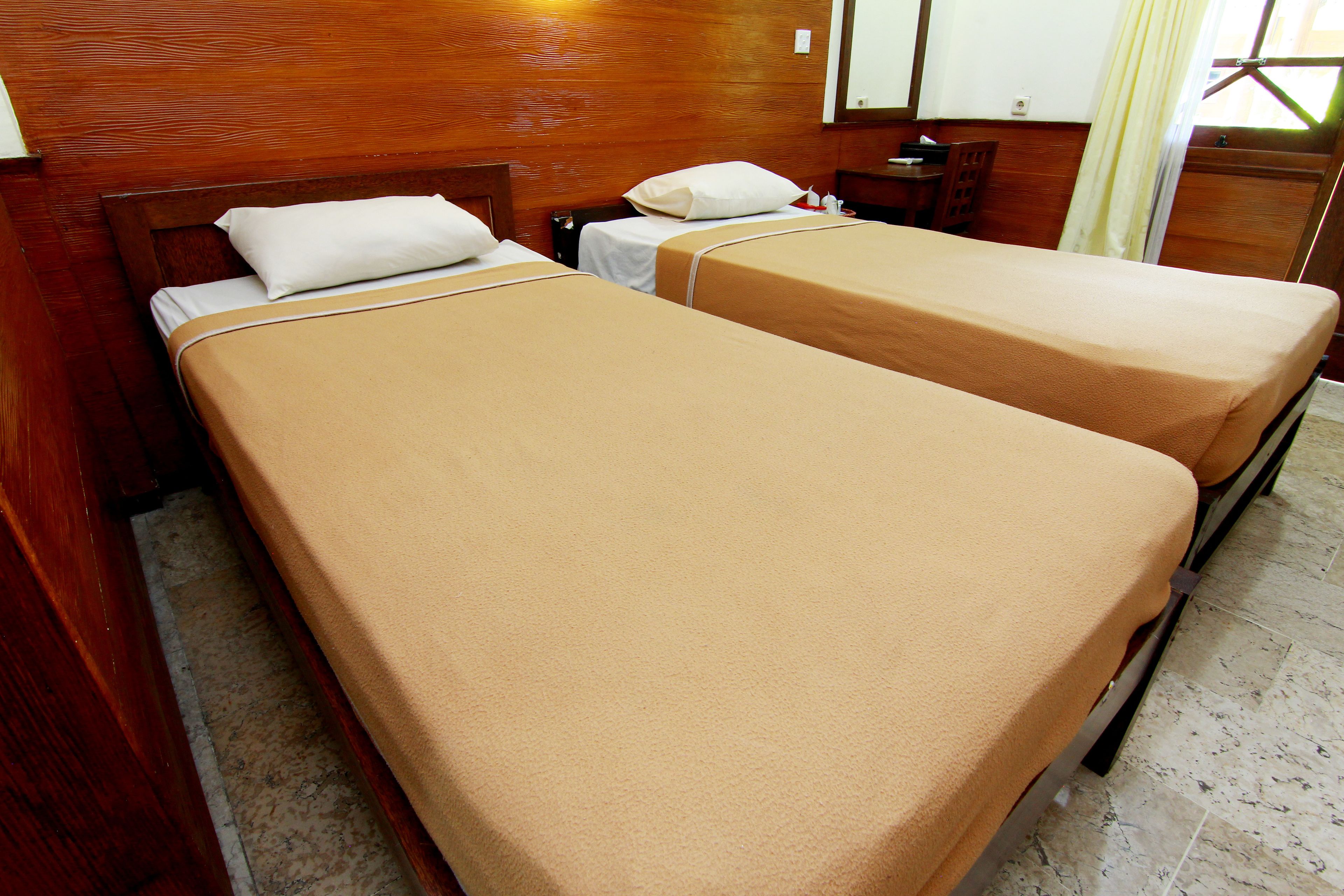 Duas camas de solteiro com roupa de cama bege num quarto com paredes de madeira e chão em mosaico.