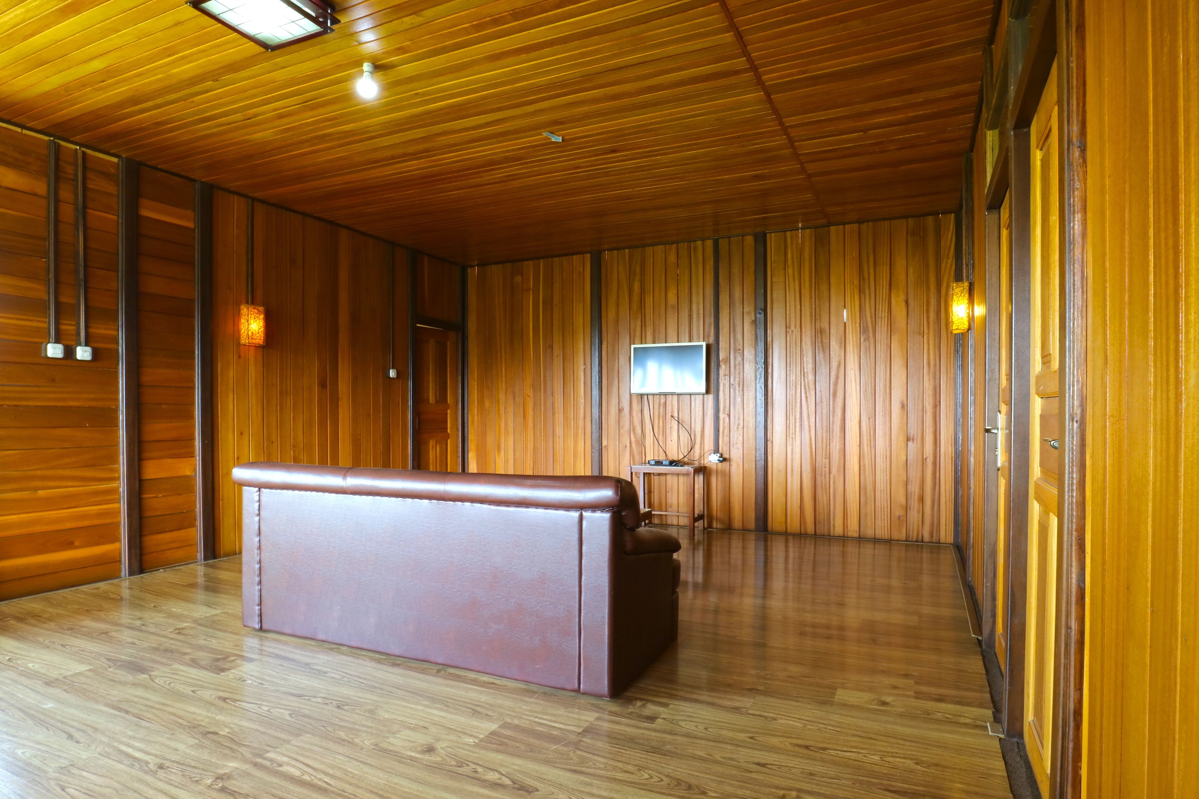 Quarto com paredes de painel de madeira, um banco de couro marrom, uma televisão de tela plana e uma mesinha com um abajur.