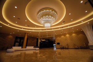 Um hall amplo com um lustre grande e ornamentado, um balcão de recepção branco e uma área de estar com sofás.