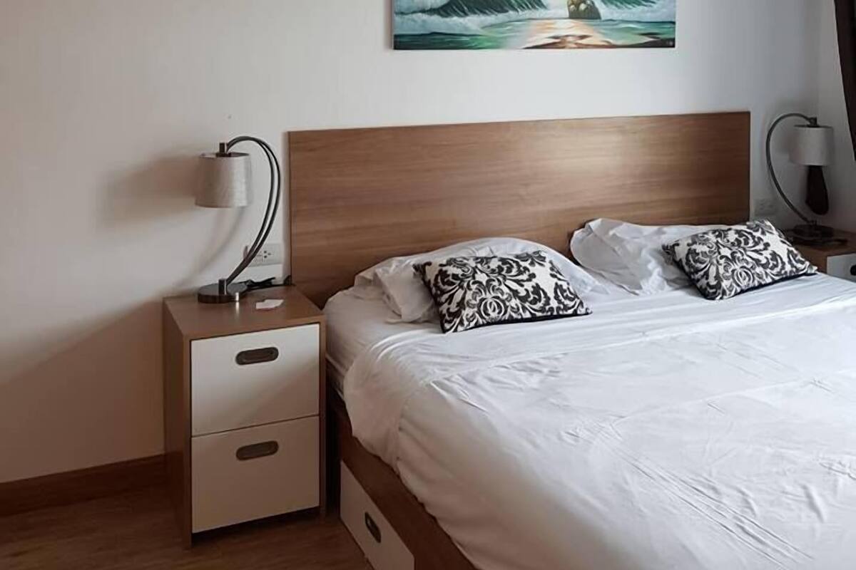 Quarto com uma cama, mesas de cabeceira, uma luminária, um quadro e um ar condicionado.