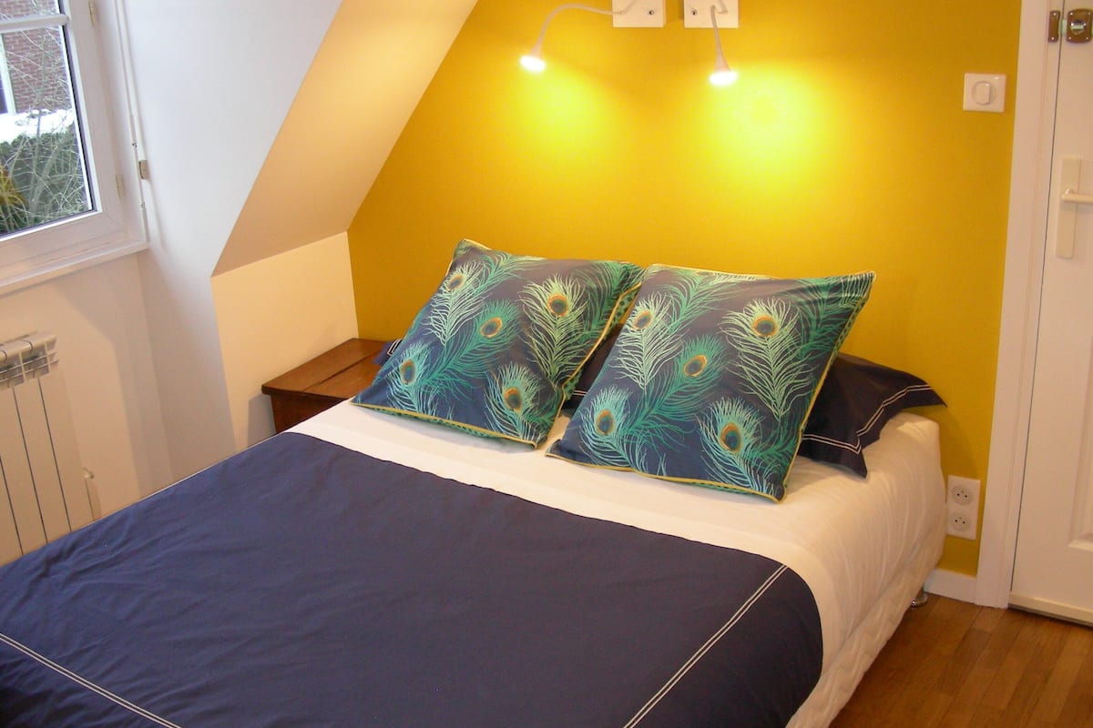 Quarto com cama, duas almofadas com tema de pavão, mesa de cabeceira e janela com vista.