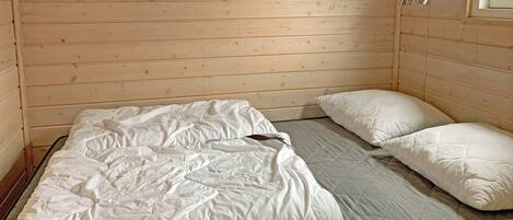 Um quarto pequeno com painéis de madeira, uma cama simples, um travesseiro e uma mesa de cabeceira.