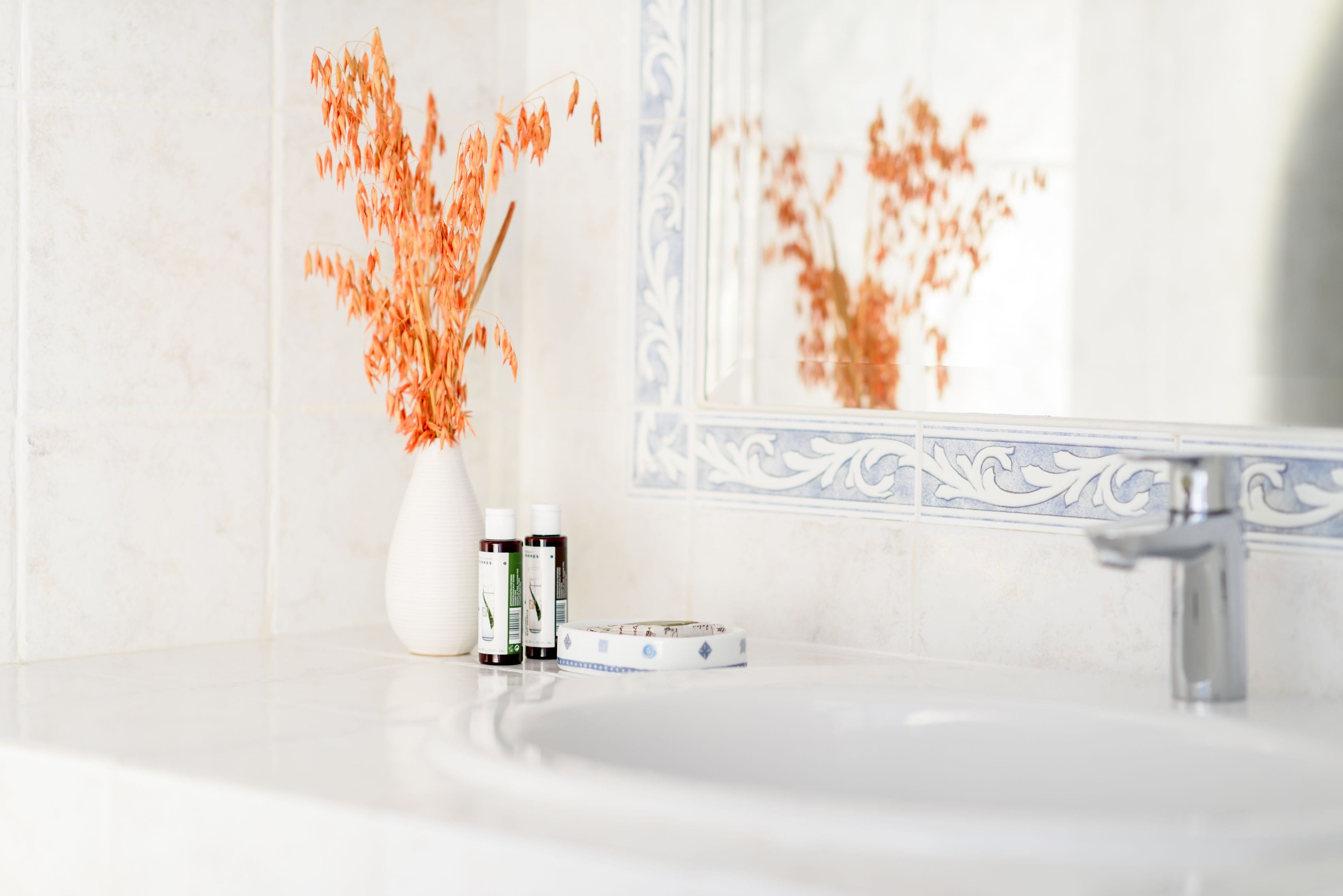 Um banheiro com pia branca, um vaso com flores secas e duas embalagens de loção.