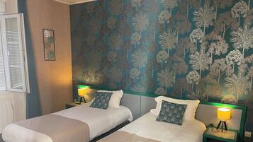 Quarto de hotel com duas camas, cada uma com mesa de cabeceira e luminária, e um papel de parede estampado.