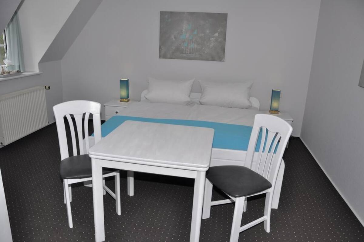 Quarto com cama, duas mesas de cabeceira, escrivaninha e duas cadeiras.