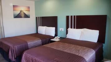 Quarto de hotel com duas camas, cada uma com cabeceira e travesseiro. Há um quadro na parede e um telefone na mesa de cabeceira.