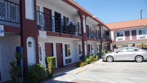 Um motel de dois andares com fachada vermelha e branca, várias varandas e um estacionamento.