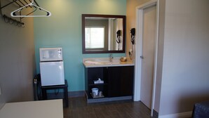 Casa de banho compacta com lavatório branco, espelho, secador de cabelo e micro-ondas.