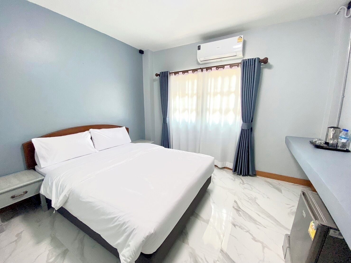 Quarto de hotel com cama, mesa de cabeceira, ar condicionado e escrivaninha com cadeira.