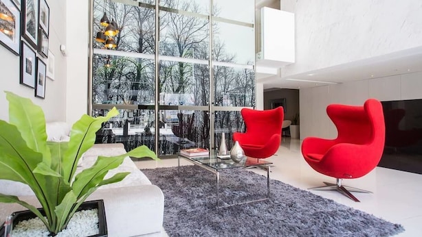 Uma sala de estar moderna com parede de vidro, cadeiras vermelhas e uma planta grande.