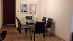 Uma área de refeições com uma mesa de vidro cercada por cadeiras pretas, um vaso com flores e dois espelhos emoldurados na parede.