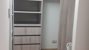 Um closet espaçoso com várias prateleiras e gavetas, uma porta branca e um interruptor de luz na parede.
