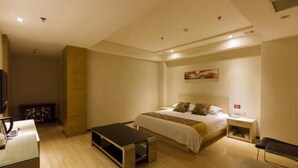 Quarto de hotel moderno com cama, mesa de cabeceira e pequena escrivaninha com cadeira.