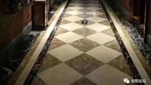 Um corredor com piso xadrez, paredes de tijolo e teto iluminado em azul.