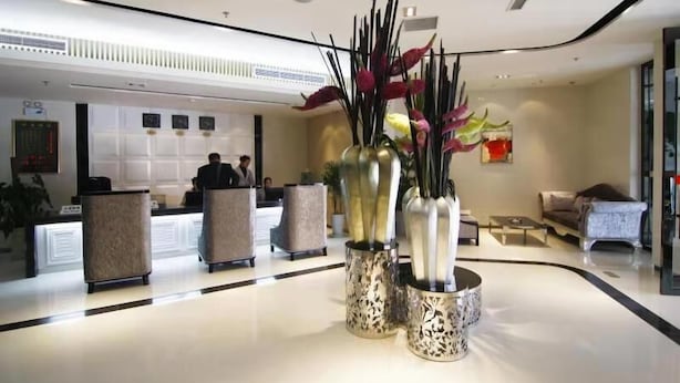 Um hall de hotel moderno, com balcão de recepção, área de estar e vasos decorativos com plantas altas.