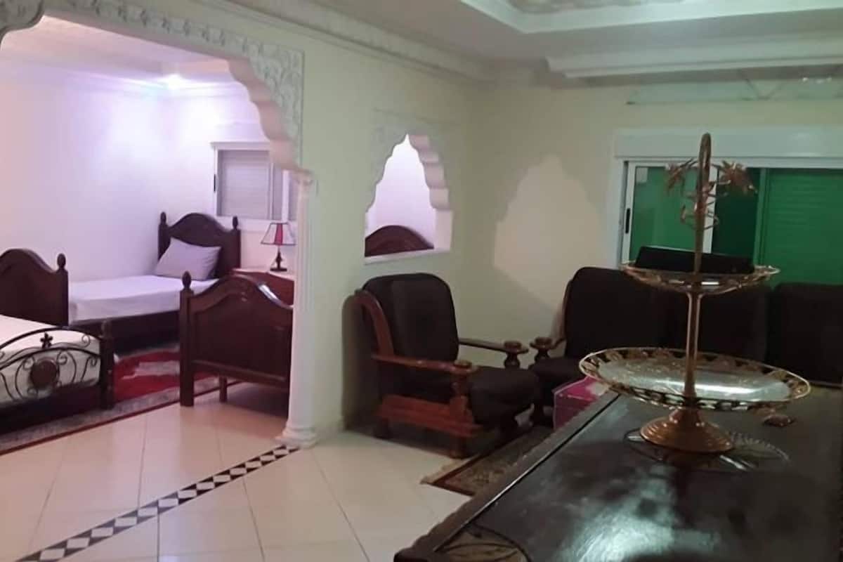Quarto com cama, poltrona, sofá e mesa com um objeto decorativo.