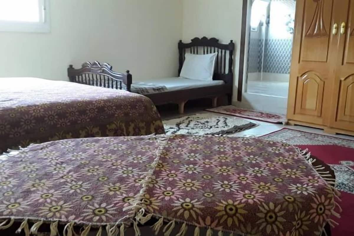 Quarto com duas camas, um guarda-roupa de madeira e um tapete estampado.
