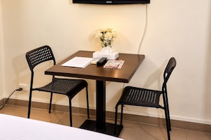 Quarto de hotel com uma mesa, duas cadeiras, um controle remoto, uma caixa de lenços e um vaso com flores.