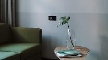 Sala de estar moderna com um sofá verde, uma mesa de centro de madeira com uma planta e um livro, uma luminária pendente branca e um aplique de parede.