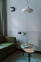 Sala de estar moderna com um sofá verde, uma mesa de centro de madeira com uma planta e um livro, uma luminária pendente branca e um aplique de parede.