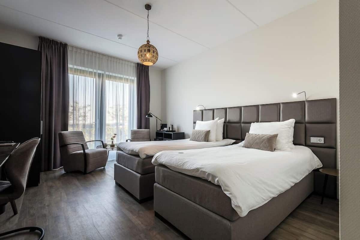 Quarto de hotel moderno com duas camas, uma mesa e uma cadeira.