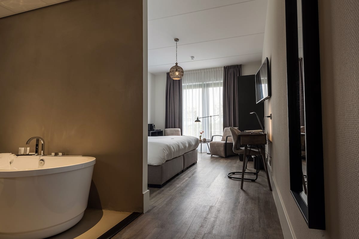 Quarto de hotel moderno com uma banheira grande, uma cama, uma escrivaninha e uma televisão.